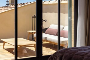 Uma varanda com mesa e cadeiras de madeira, um sofá com almofadas e vista para o exterior do edifício.