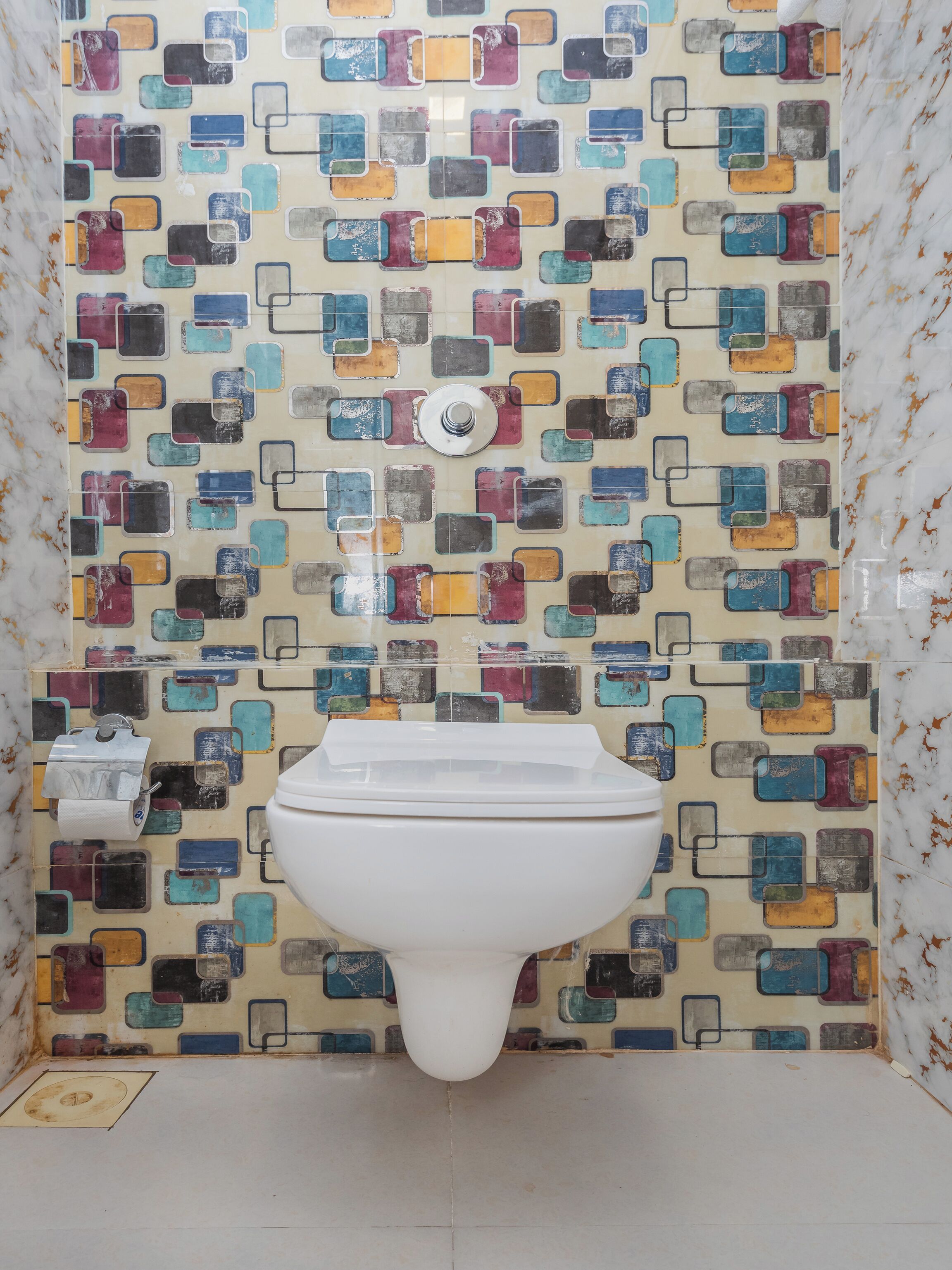 Casa de banho com sanita branca, parede estampada e suporte para papel higiénico.