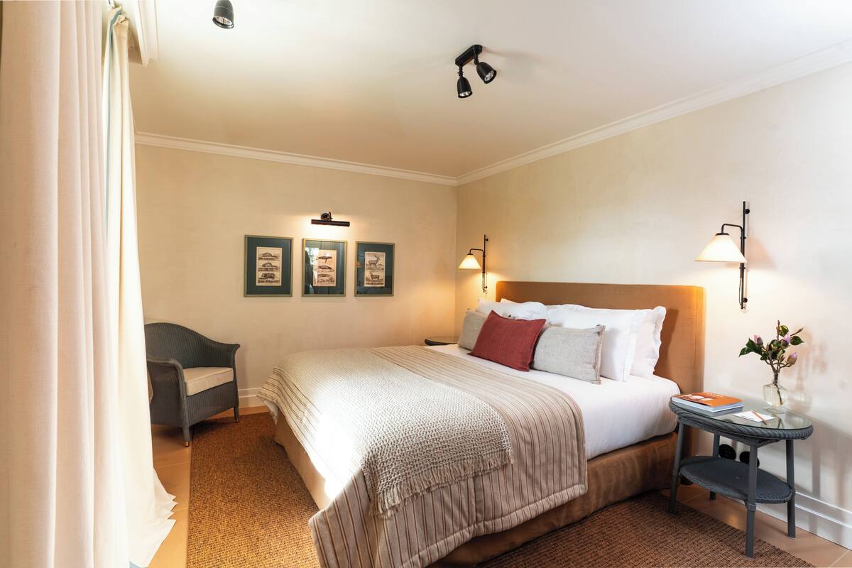 Quarto de hotel com cama, mesa de cabeceira, luminária e obra de arte na parede.