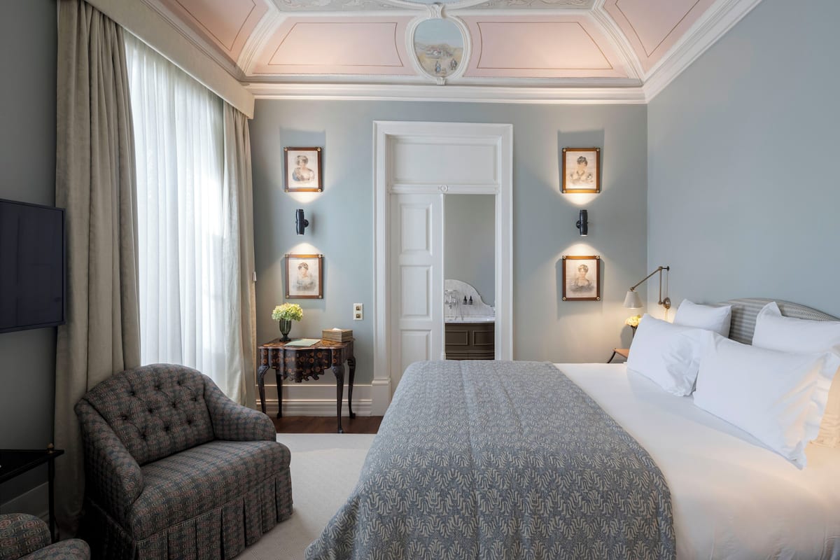 Quarto de hotel com uma cama grande, uma cadeira, uma escrivaninha e uma televisão.