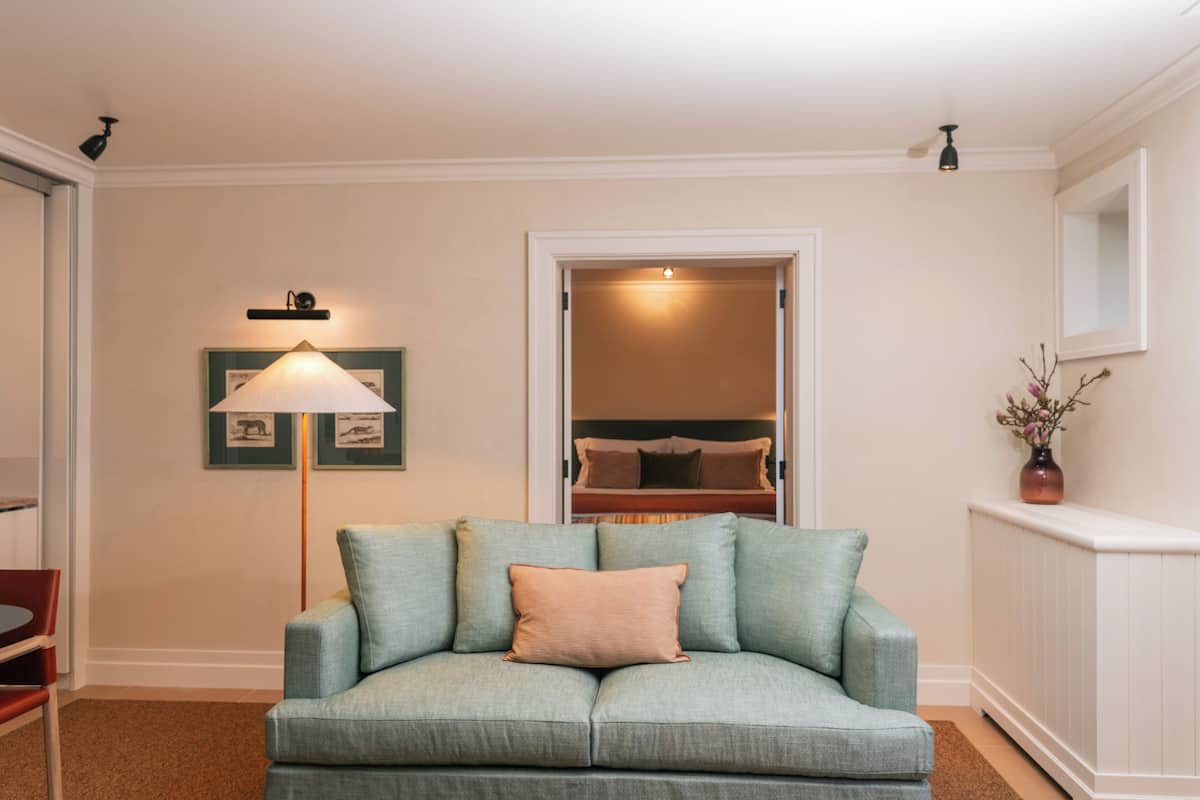Uma sala de estar com um sofá verde-clarinho, luminária de chão, quadro emoldurado e radiador.