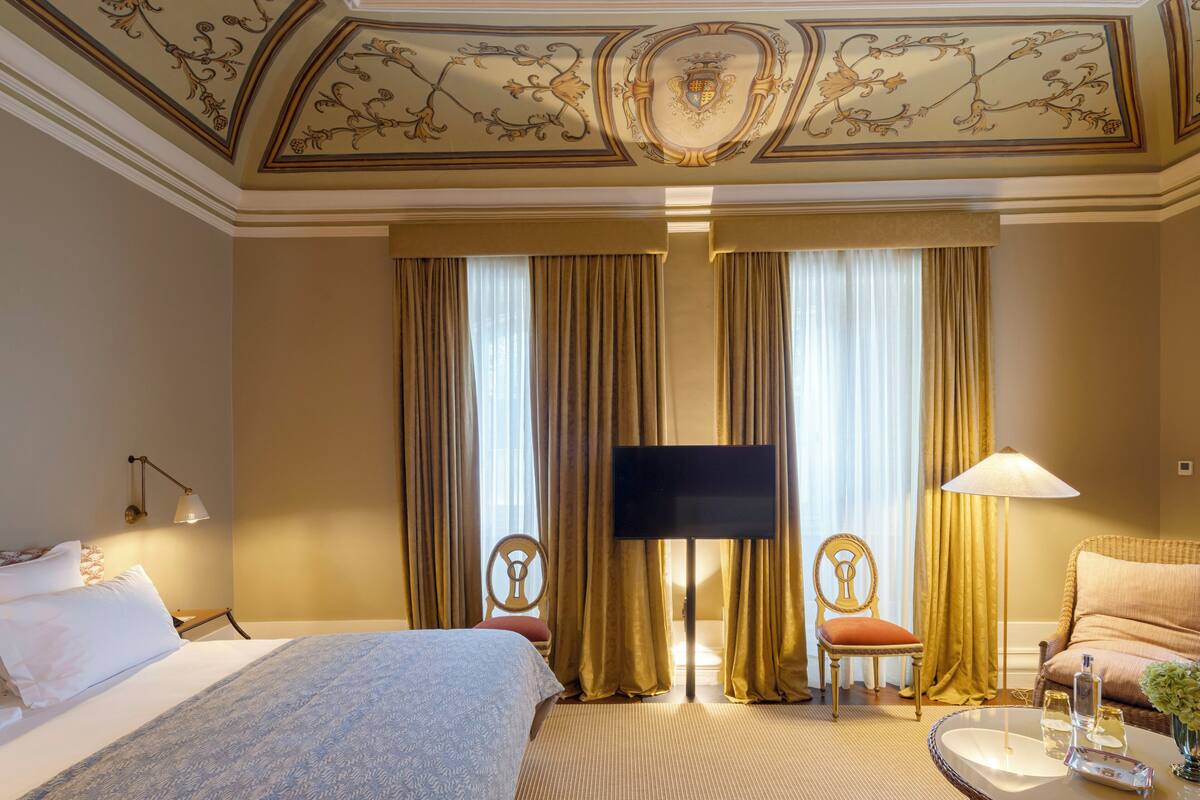 Quarto de hotel com cama, televisão, poltrona, sofá e mesa com bandeja.