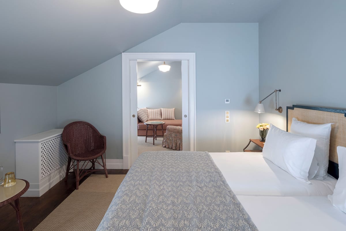 Quarto com cama, uma cadeira, escrivaninha e uma mesinha de cabeceira com abajur.