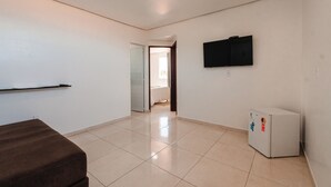 Quarto com uma cama, televisão fixada na parede, geladeira e porta que dá para outro cômodo.