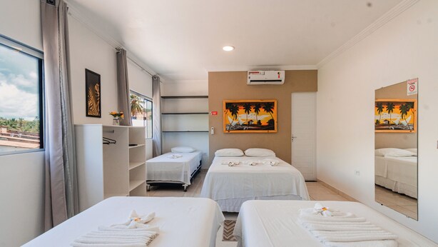 Quarto de hotel com duas camas, uma janela grande com cortinas, um quadro na parede e um aparelho de ar condicionado.