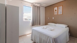 Quarto de hotel com cama, janela com cortinas, obra de arte na parede e iluminação no teto.