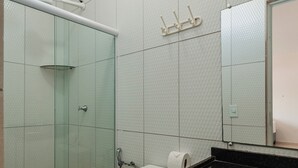 Um banheiro com box de vidro, vaso sanitário, pia com bancada preta e espelho sobre a pia.