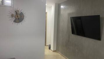Uma sala de estar moderna com uma grande televisão de tela plana na parede, um relógio de sol com design único e um console branco minimalista.