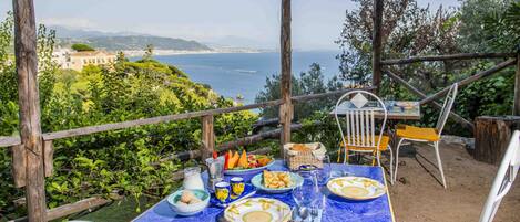 Área externa com mesa posta para dois, com vista para a paisagem costeira.