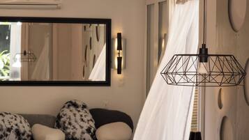 Quarto moderno com cama, espelho grande, luminária pendente e mesa de vidro com cadeiras.