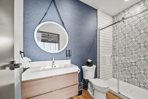 Casa de banho moderna com espelho redondo, lavatório branco e chuveiro com azulejos estampados.