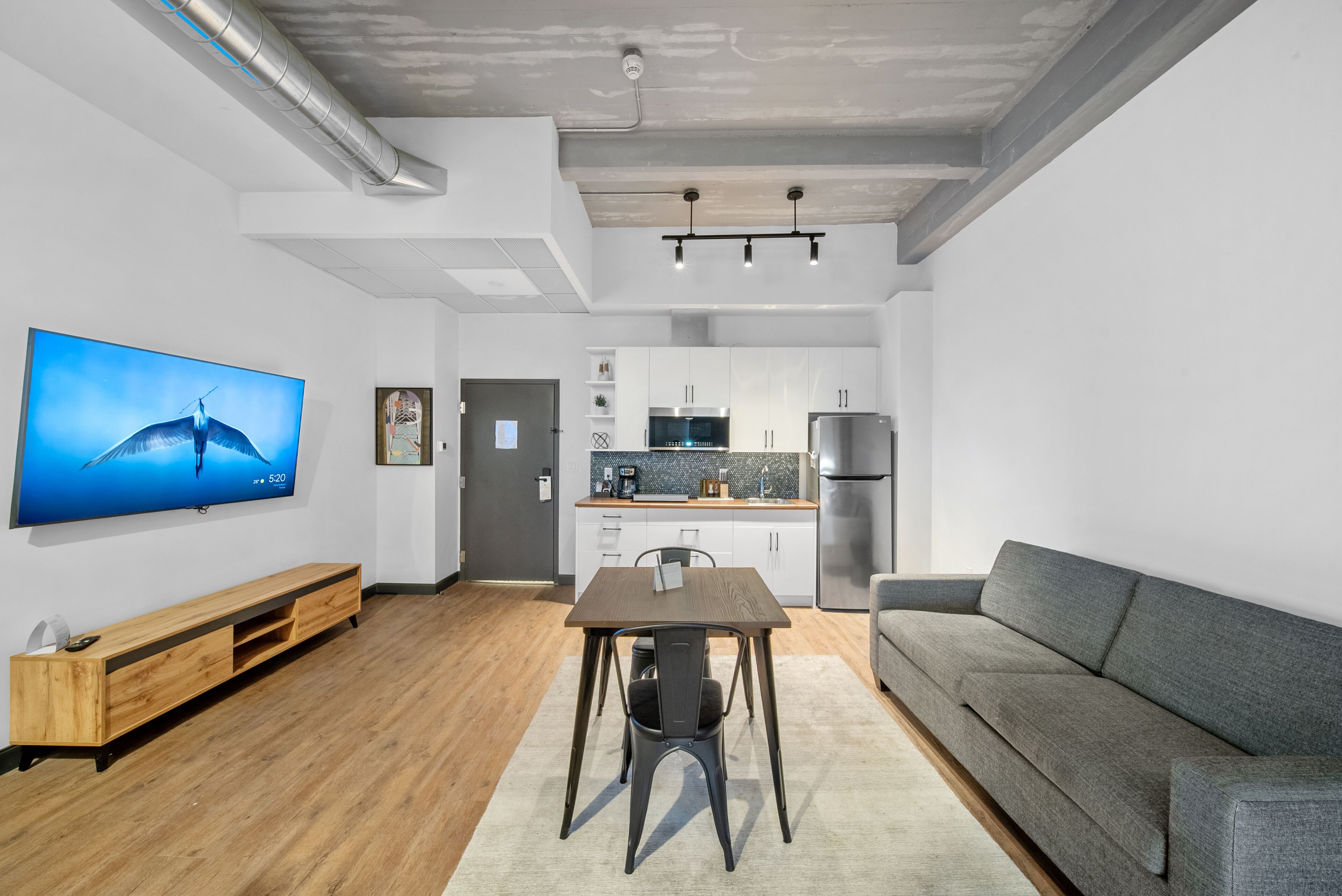 Uma sala de estar moderna com televisão de tela plana, móvel de entretenimento de madeira, sofá cinza e mesa de jantar com cadeiras.