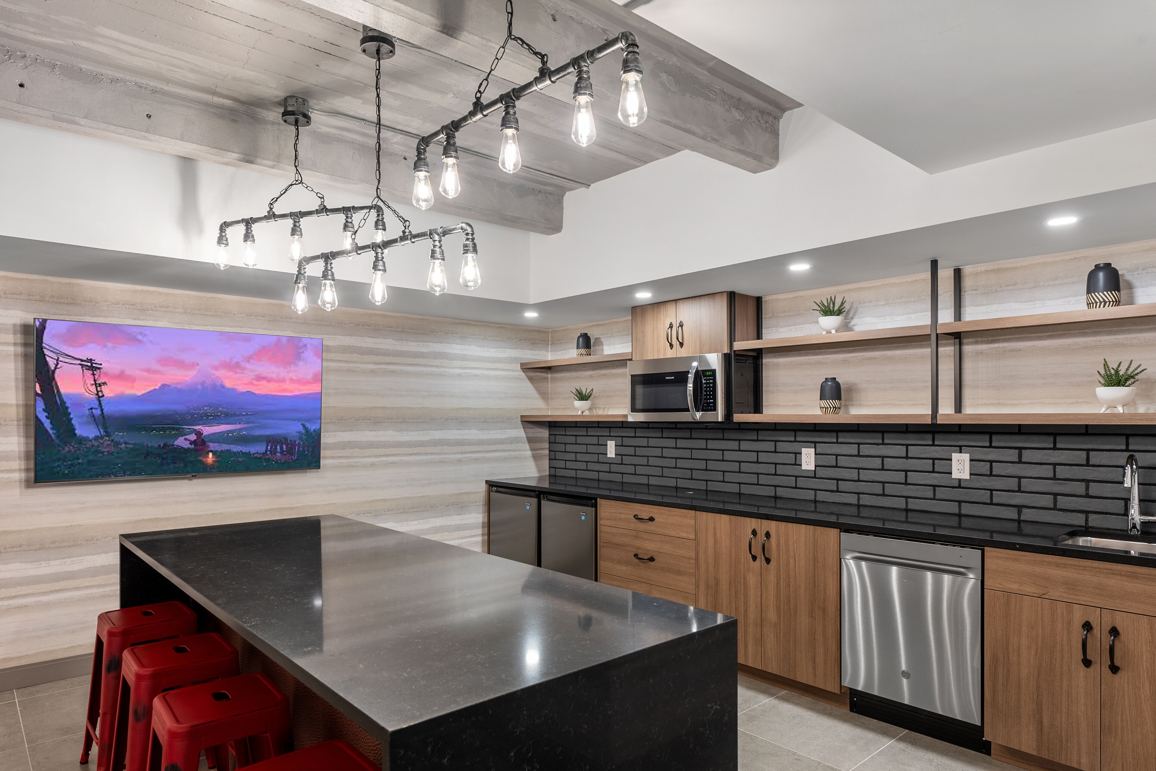 Cozinha moderna com bancada preta, armários de madeira e painel de fundo preto. Há uma ilha grande com banquetas vermelhas, uma lava-louças de aço inoxidável e um micro-ondas preto.