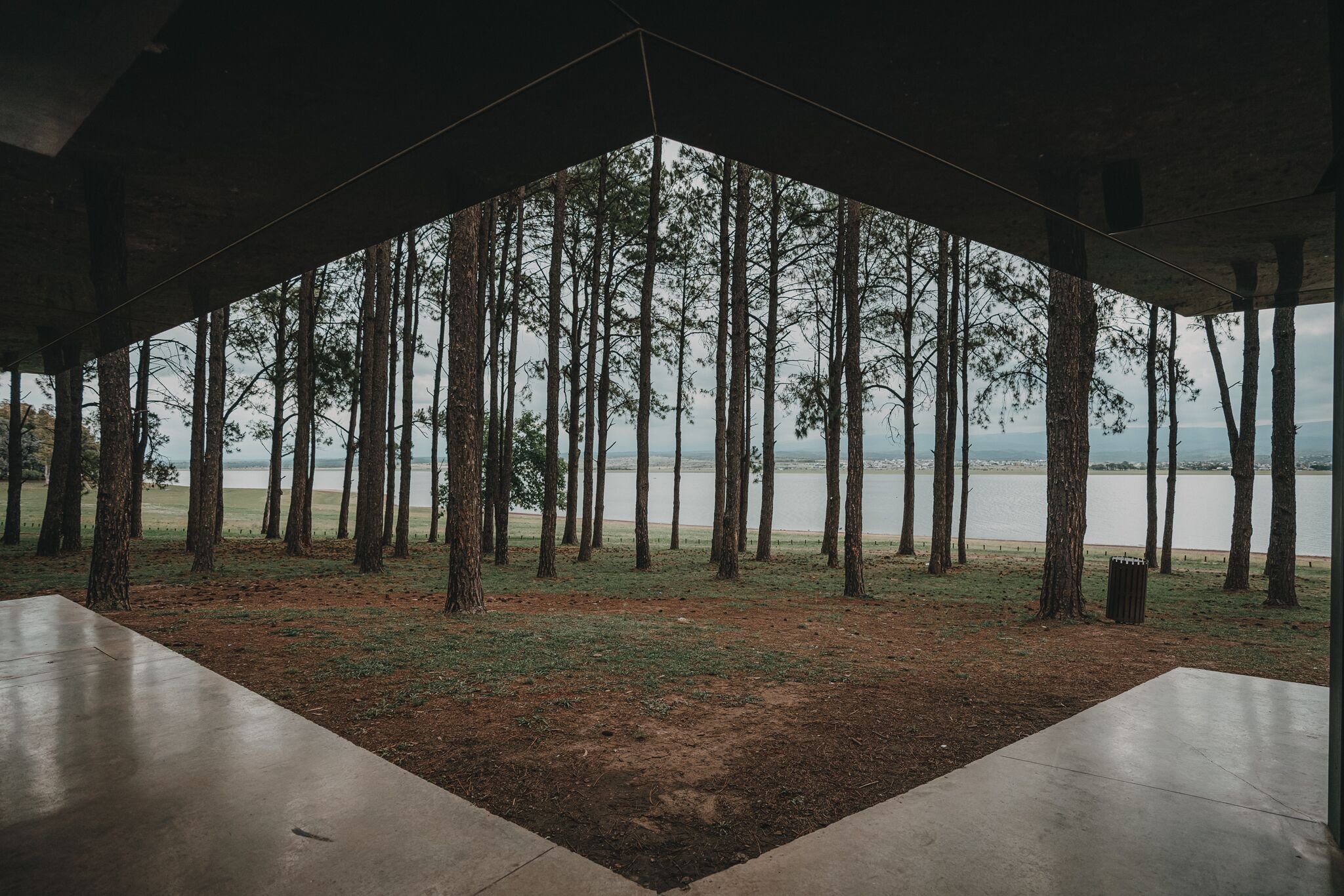 Um pavilhão aberto com vista para um lago e árvores.