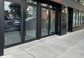 Entrada de hotel com portas de vidro, estacionamento e fachada do edifício.