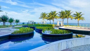 Área de piscina com palmeiras, uma espreguiçadeira e vista para o oceano.