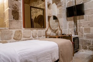 Quarto com parede de pedra, cama, televisão montada na parede e espelho sobre a cama.