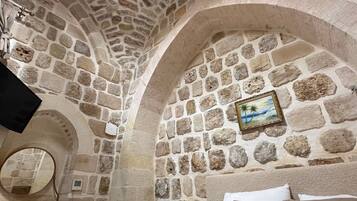 Quarto com paredes de pedra, uma cama, um espelho e um quadro na parede.
