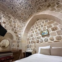 Quarto com paredes de pedra, uma cama, um espelho e um quadro na parede.