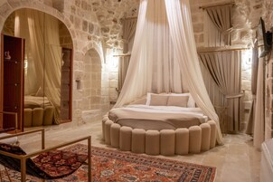 Quarto com cama redonda, dossel, paredes de pedra e um espelho grande.