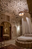 Quarto com paredes de pedra, uma cama, um espelho e um candeeiro pendente.