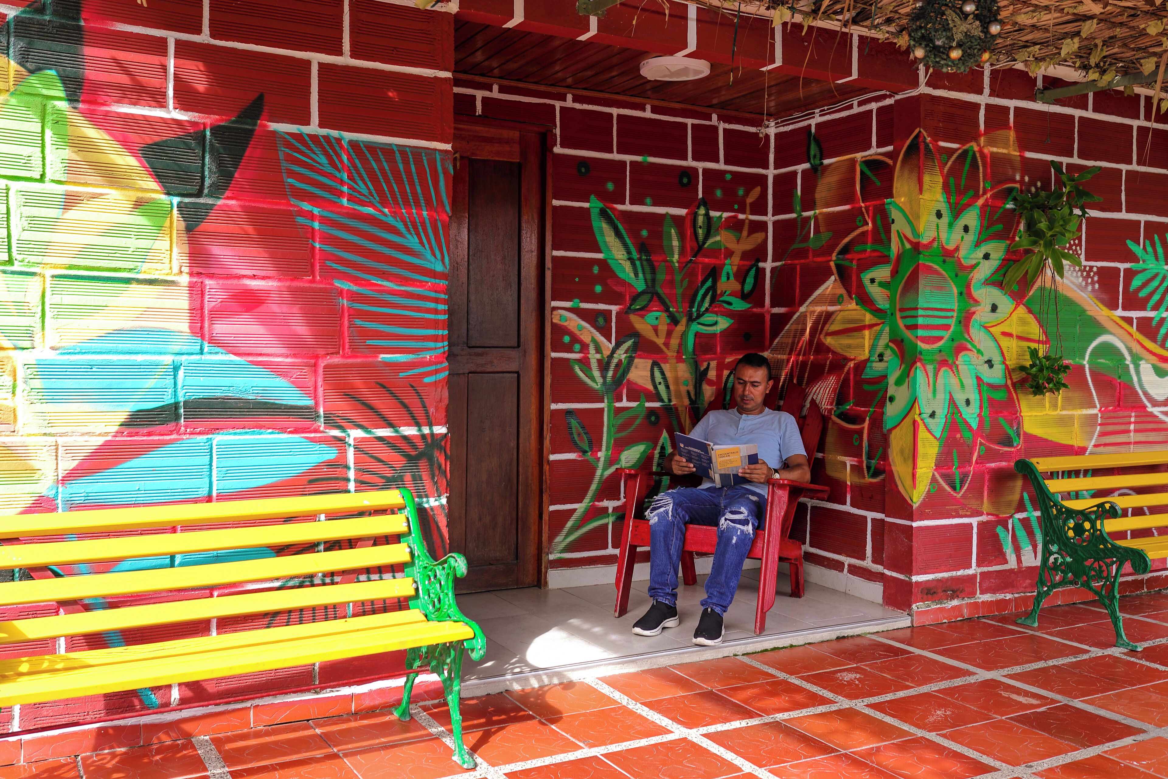 Um homem sentado em um banco vermelho em frente a um prédio com murais coloridos nas paredes.