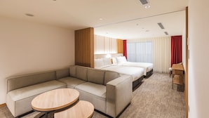 Quarto de hotel com sofá, duas mesas redondas, cama e escrivaninha.