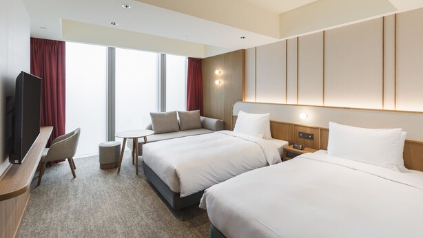 Quarto de hotel com duas camas, televisão, escrivaninha e uma mesinha.