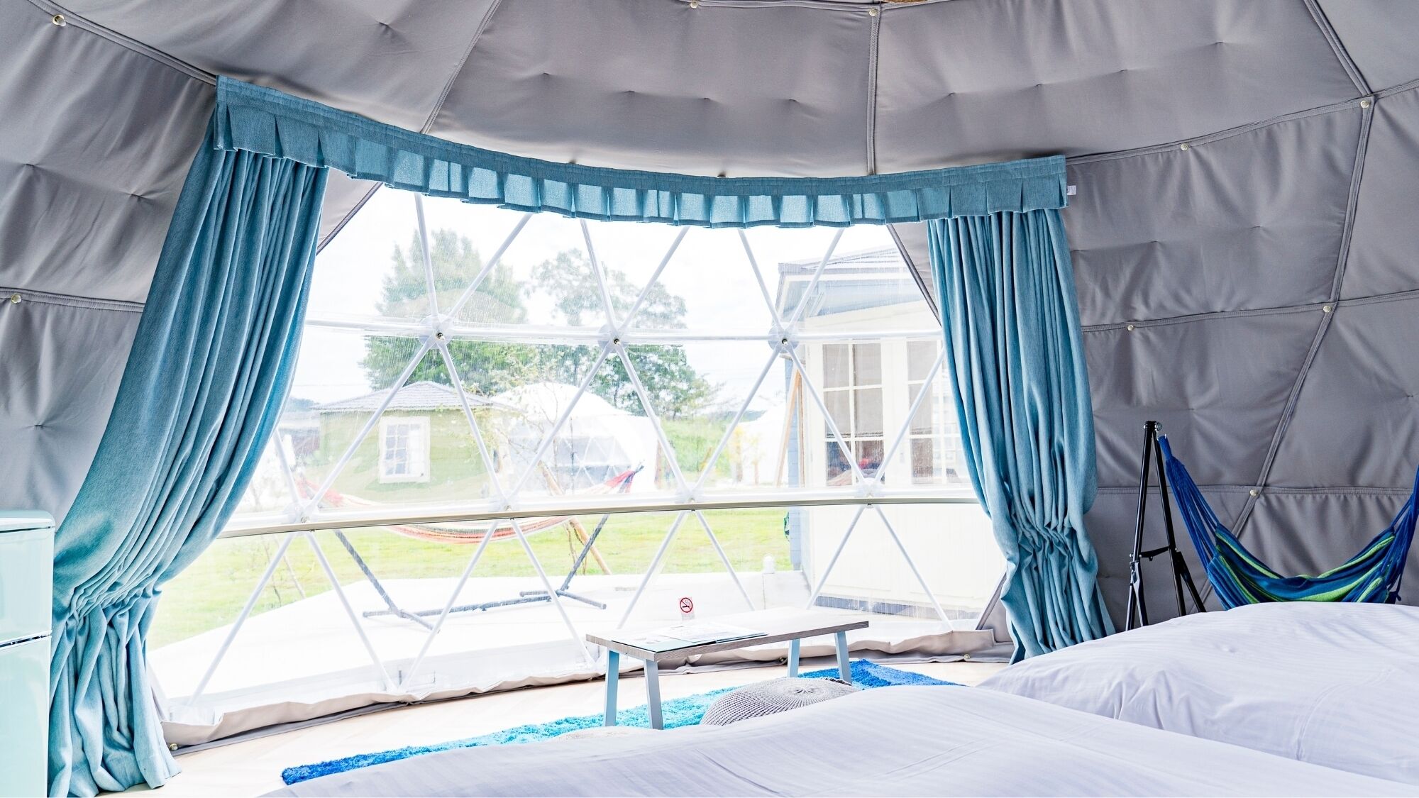 Um quarto tipo tenda com cama, mesa e rede.