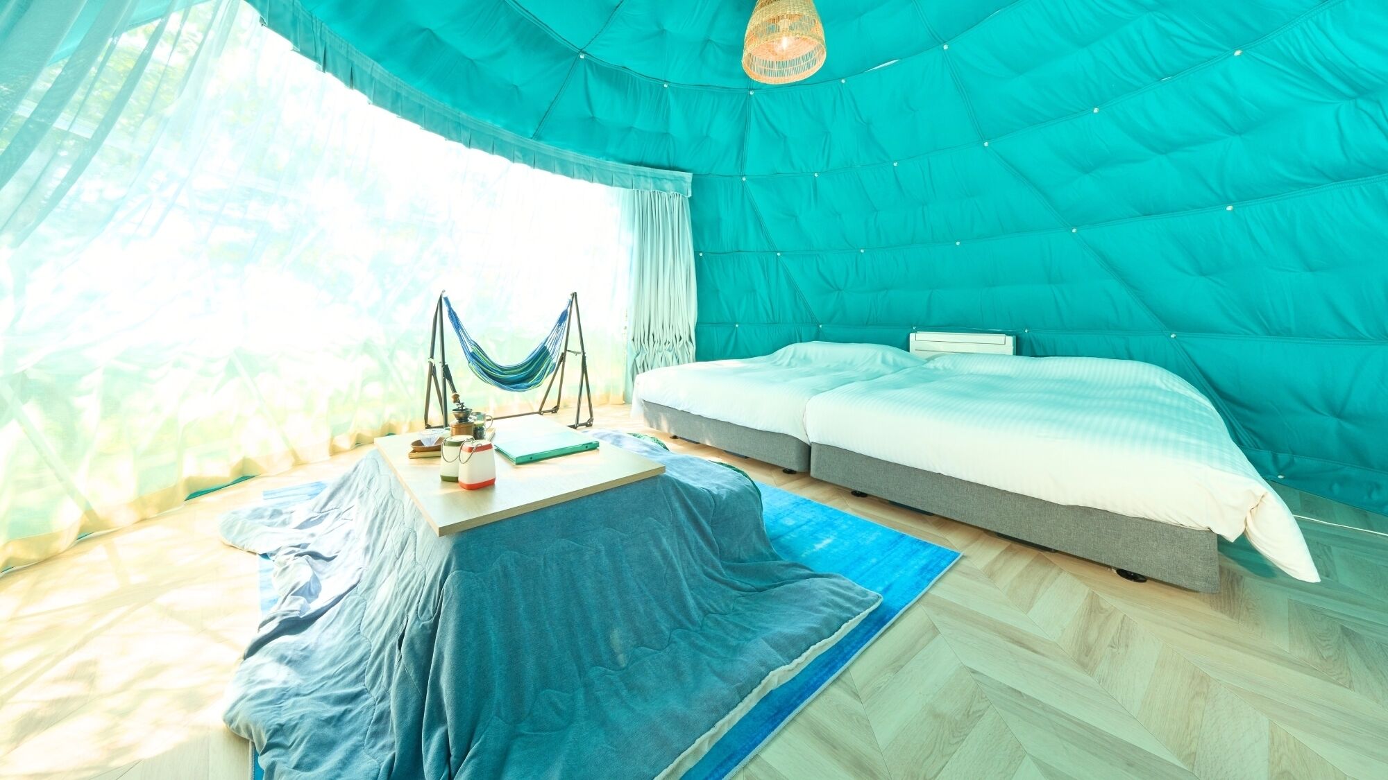 Quarto tipo tenda com uma cama, uma mesa com objetos e uma rede.