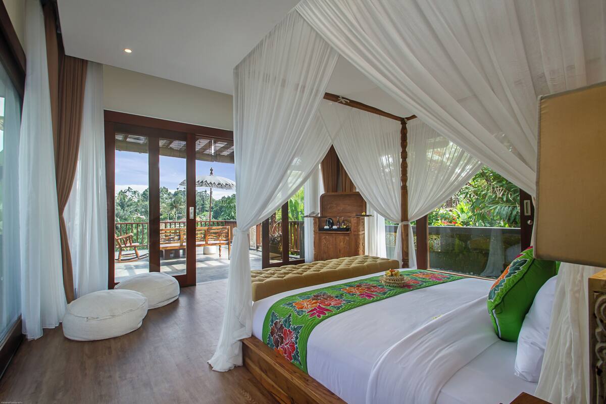 Quarto com uma cama grande, um banco de madeira e vista para um jardim.