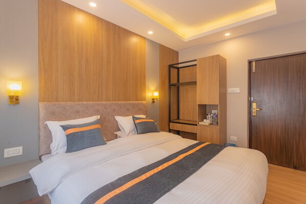 Quarto de hotel moderno com uma cama grande, cabeceira de madeira, estantes embutidas e um guarda-roupa.