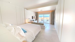 Quarto de hotel moderno com uma cama grande, uma escrivaninha com cadeira e vista para a praia pela janela.