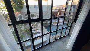 Quarto com uma grande janela vista para uma piscina e um pátio com mobiliário de exterior.
