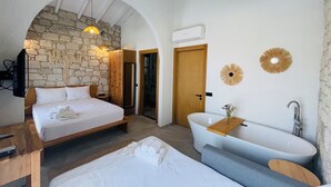 Quarto com parede de pedra, porta de madeira, banheira e cama com toalhas enroladas.