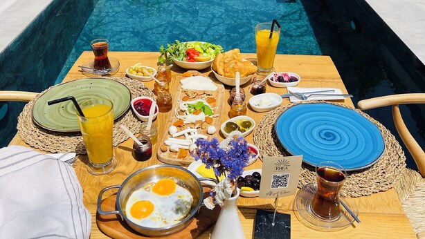 Café da manhã à beira da piscina, com mesa, cadeiras e piscina.