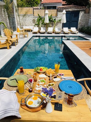 Café da manhã à beira da piscina, com mesa, cadeiras e piscina.