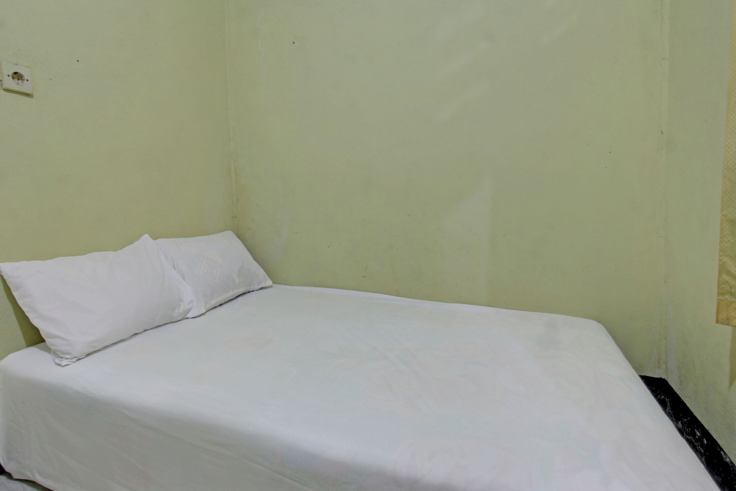 Quarto pequeno com uma cama de solteiro, coberta por um lençol e travesseiros brancos.