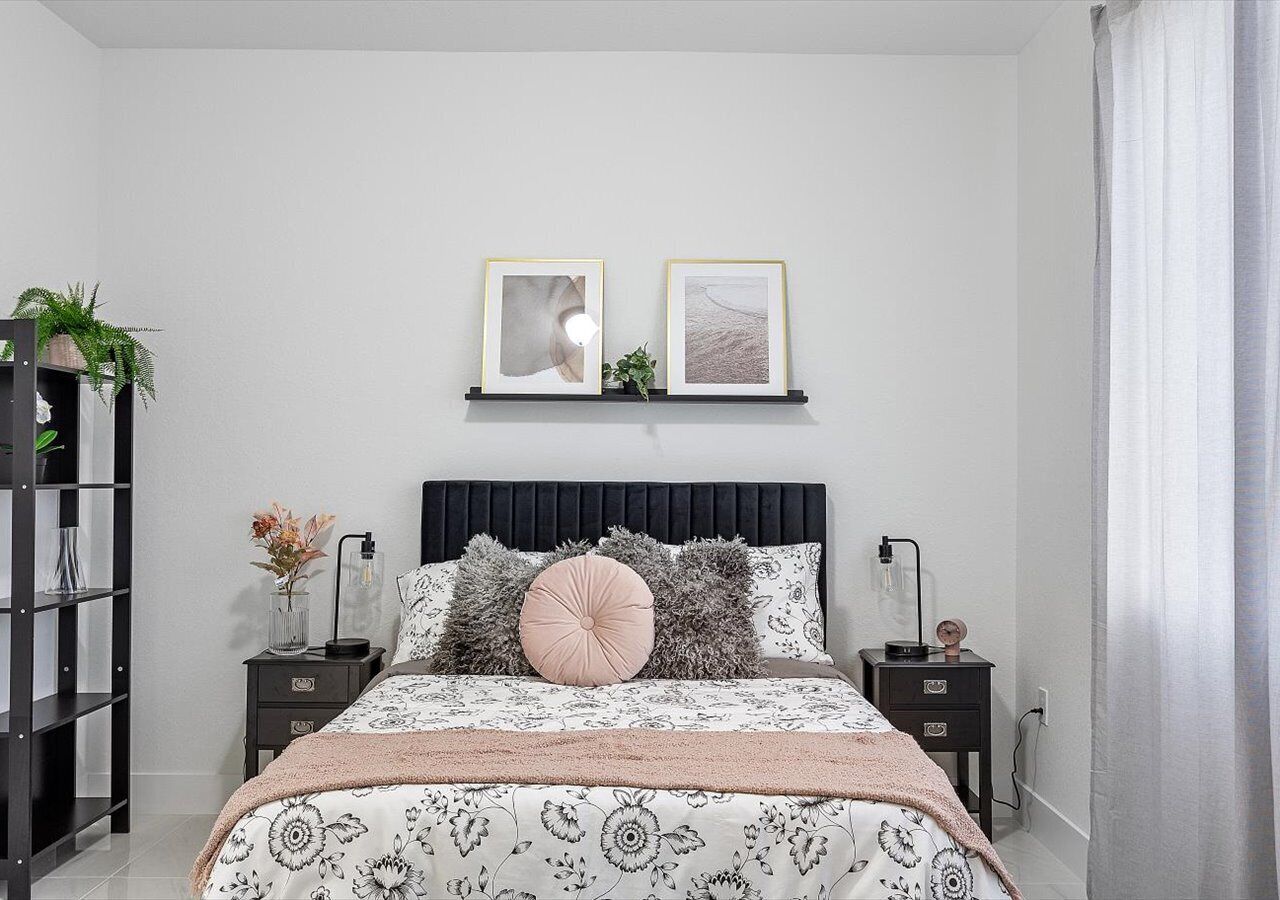 Quarto com cama, mesas de cabeceira, uma estante com quadros e uma planta.