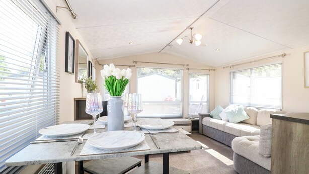Interior moderno de uma motorhome, com área de refeições, assentos e um vaso com flores.