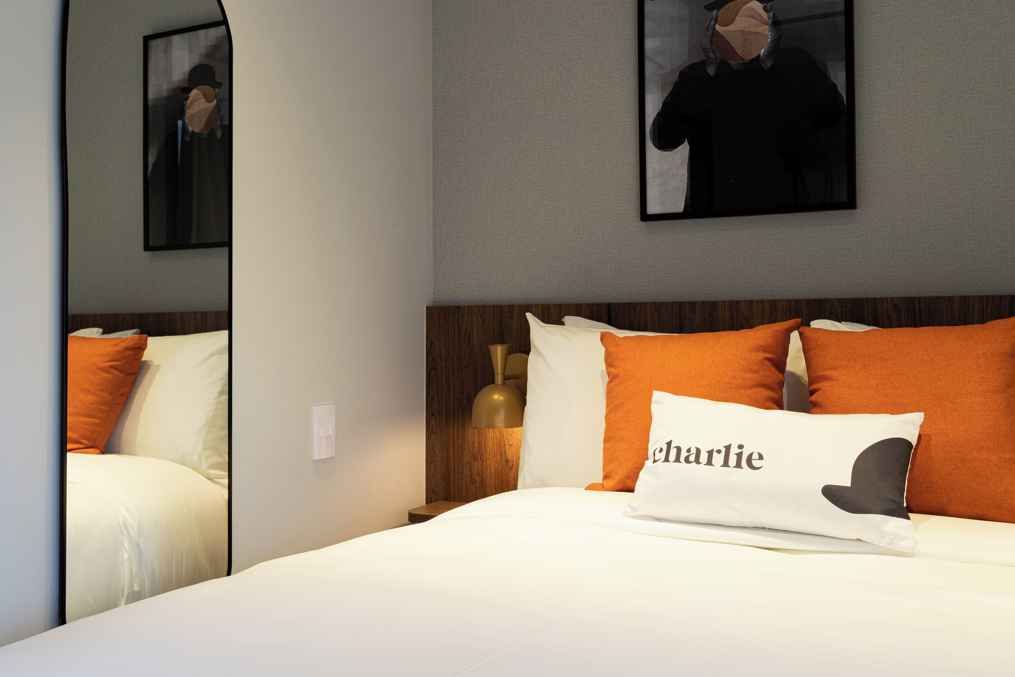 Quarto de hotel com cama bem arrumada, espelho na parede e quadro emoldurado sobre a cama.