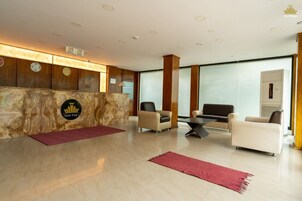 Uma área de recepção de hotel, com um balcão de mármore, um relógio e uma sala de estar com sofás e uma mesa de centro.