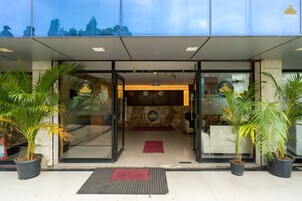 Uma entrada de hotel moderna com portas de vidro, balcão de recepção e plantas em vasos.