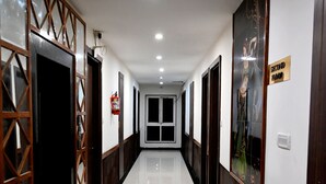 Um corredor comprido e estreito com piso lustroso, portas de madeira e uma placa na parede indicando o segundo andar.
