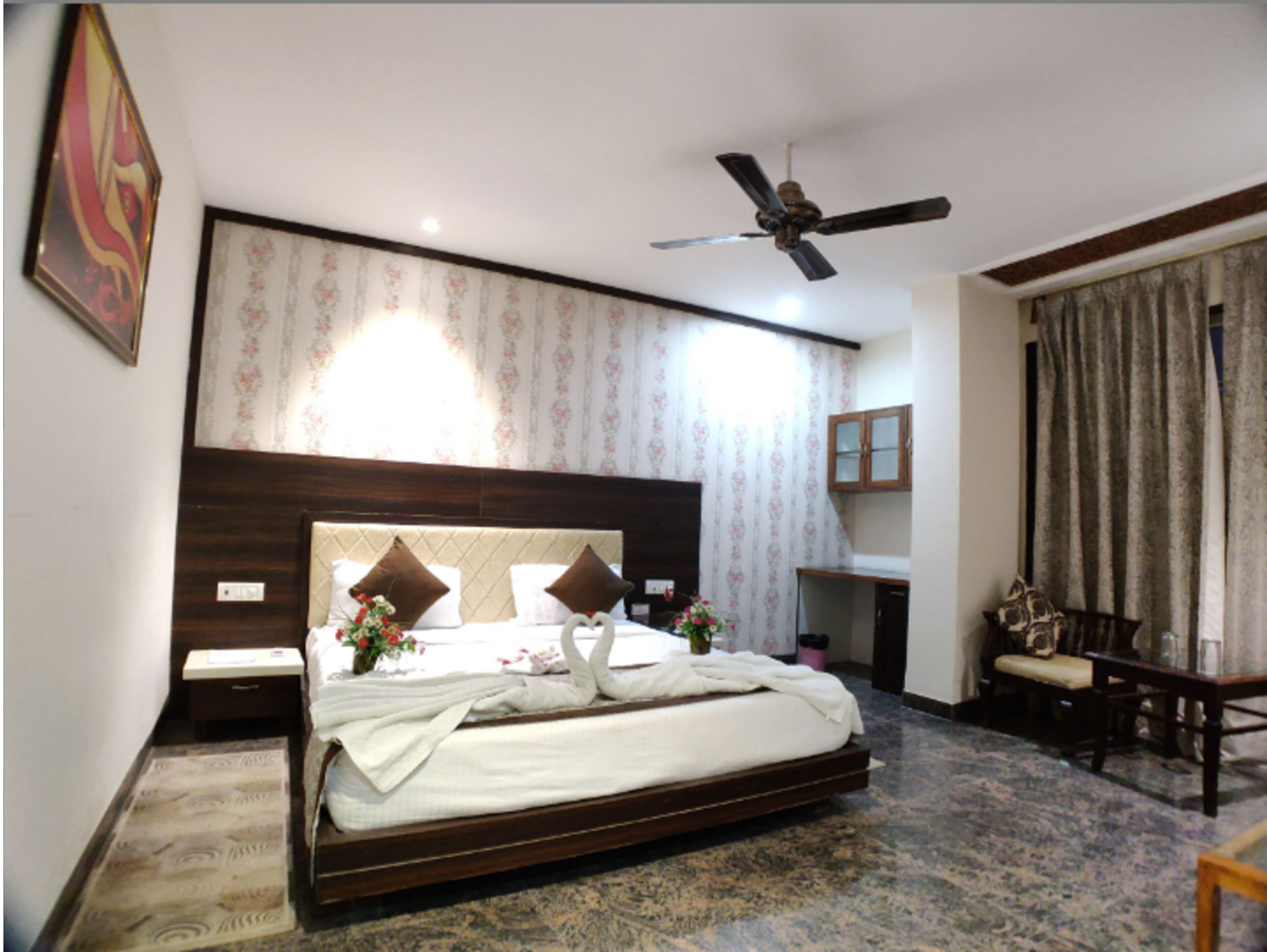 Quarto de hotel com uma cama grande, um ventilador de teto, uma mesa de cabeceira, uma escrivaninha e uma cadeira.