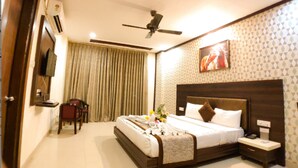 Quarto de hotel com cama, mesa de cabeceira, ventoinha no teto e televisão na parede.