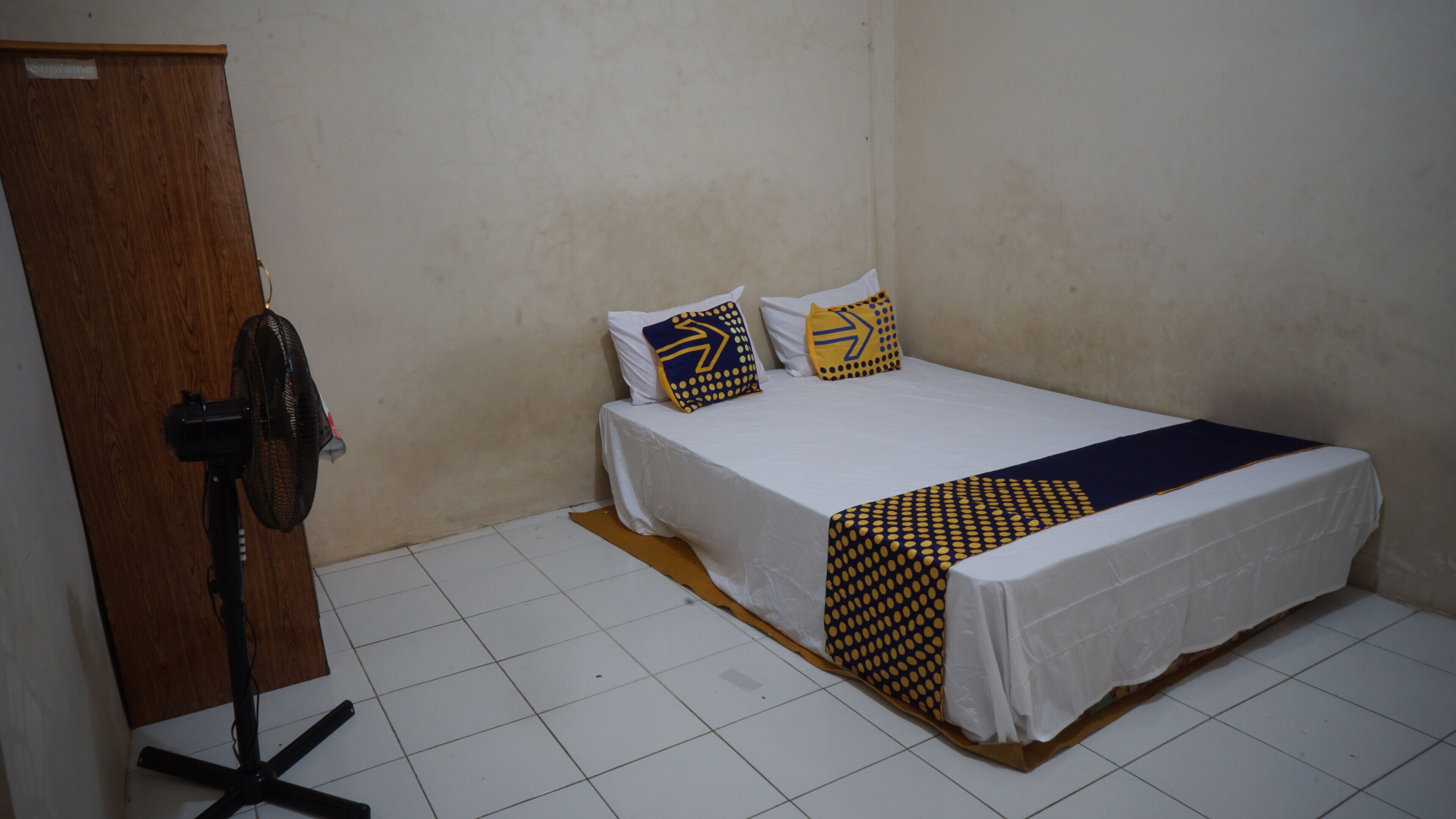 Quarto pequeno e limpo, com uma cama, um ventilador e uma porta de madeira.
