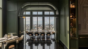 Uma sala de jantar com uma mesa posta para seis pessoas, uma grande janela em arco e vista para a cidade.