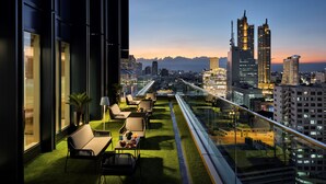 Um lounge no terraço com vista para a cidade, móveis modernos e guarda-corpo de vidro.