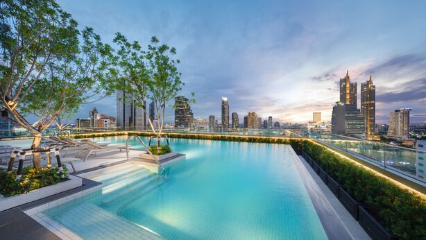 Piscina infinita no terraço com vista para o horizonte urbano, rodeada por árvores e edifícios modernos.